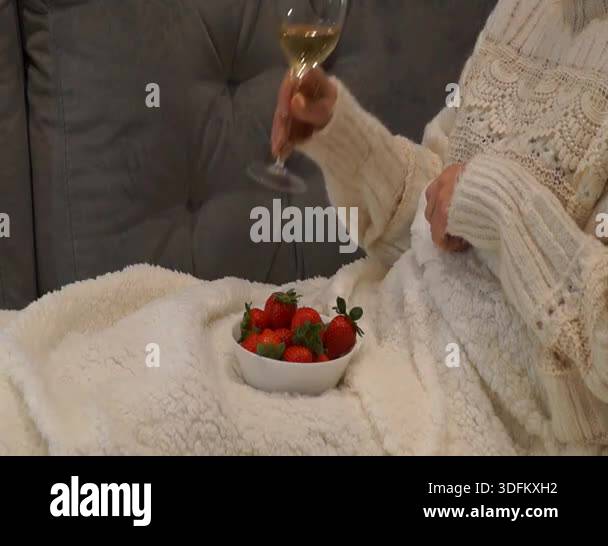 A woman relaxes on a sofa with a tray containing fresh strawberries and ...