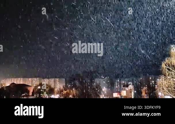 Nighttime urban scene with snow falling through a bright streetlight ...