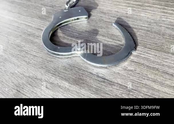 Close up of a shiny metal handcuff lying on a textured brown wooden ...