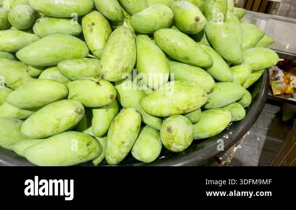 A full frame view of many green unripe mangoes piled together in a dark ...