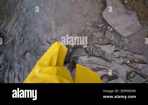 firstperson view yellow raincoat stepping on rocks near stream, boots ...