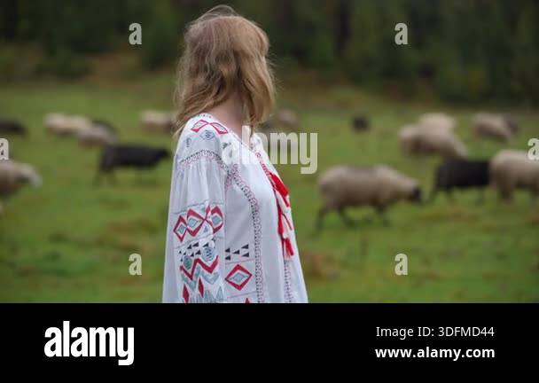 Woman in embroidered dress standing amid green pasture with grazing ...