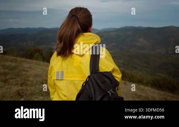 Back view hiker in yellow jacket overlooking mountain vista at dusk ...