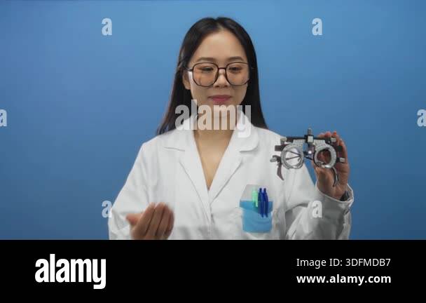 Woman optician in lab coat holds glasses against blue background ...