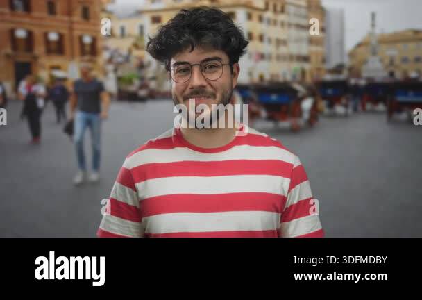 Young hispanic man with beard and glasses smiling on a bustling street ...