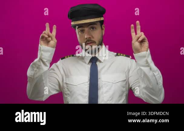 Young man with beard in pilot uniform making gesture against pink ...