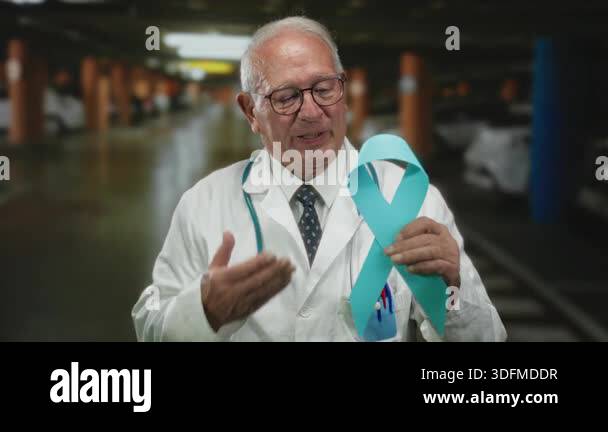 Senior male doctor holding a teal awareness ribbon in indoor parking ...