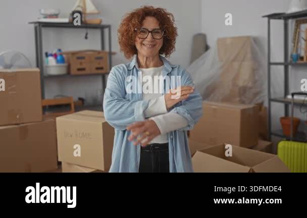 Woman smiling in living room with brown hair surrounded by moving boxes ...
