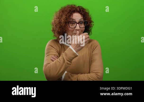Woman with glasses covering mouth in surprise against green background ...