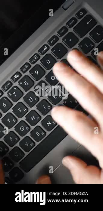 Close-up vertical image showing a persons hands actively typing on a black laptop keyboard. The ...