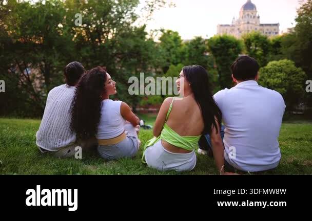 Diverse group of young friends relaxing on the green grass in a city ...