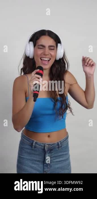 Energetic woman with headphones singing into a microphone and dancing ...