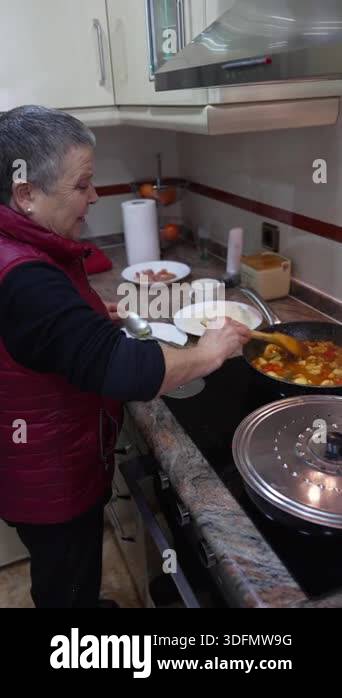Older woman with short gray hair cooking a stew in a modern kitchen ...