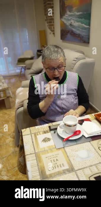 Senior woman with short gray hair and glasses eating a chocolate cookie ...