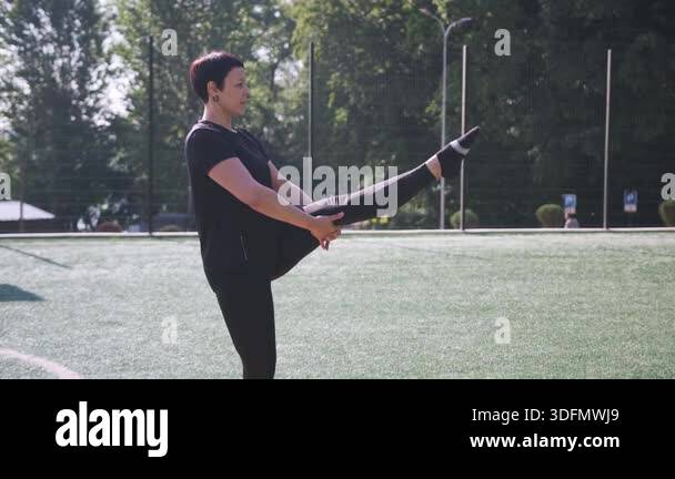 Flexible middle-aged woman performing a standing leg stretch on a green ...