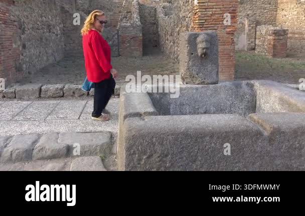 Tourist observing an ancient Roman street fountain in Pompeii ...