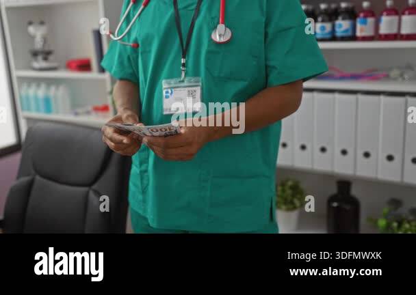Male nurse in green scrubs counting us dollars in a clinic room ...
