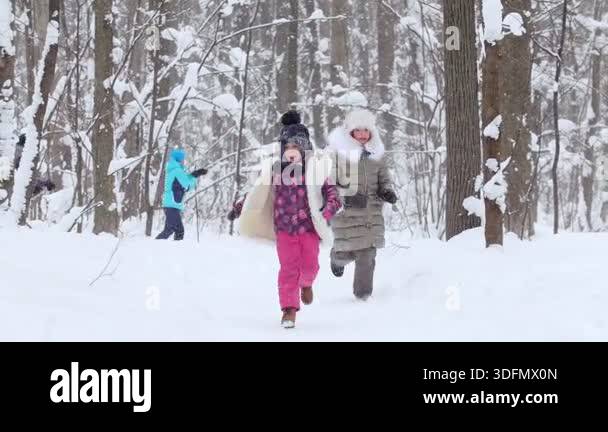Two little girls running and playing snowballs in winter forest. Mid ...