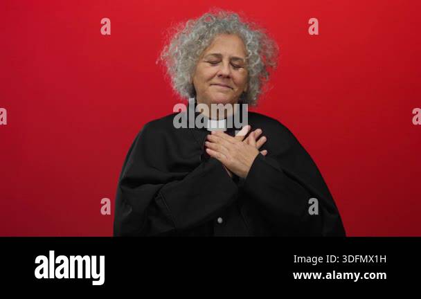Woman with grey hair wearing clergy attire and holding hand over chest ...