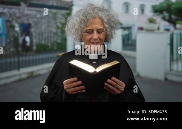 Elderly woman with grey hair in clergy attire reads a book in an urban ...