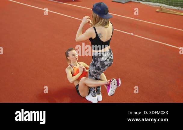 Two fit women doing sit-ups together on a stadium running track during ...