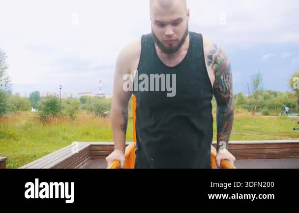 A strong man with tattoos pulling up on parallel bars on a sports ...
