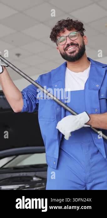Professional male mechanic in blue uniform and gloves smiling at the ...