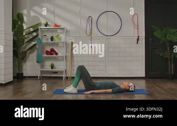 Side view of a woman in sportswear performing a pelvic lift exercise on ...