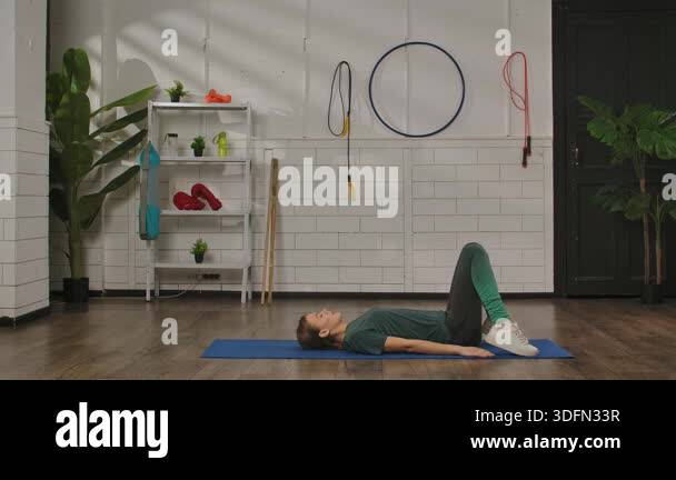 A woman performs a yoga bridge pose on a blue mat in a gym, surrounded ...
