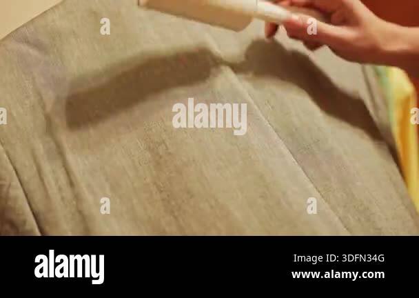 A close up of a hand using a lint roller to clean a woolen jacket ...