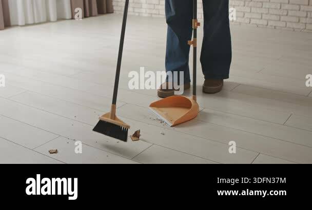 A person in jeans and shoes sweeping a light wood floor with a broom ...