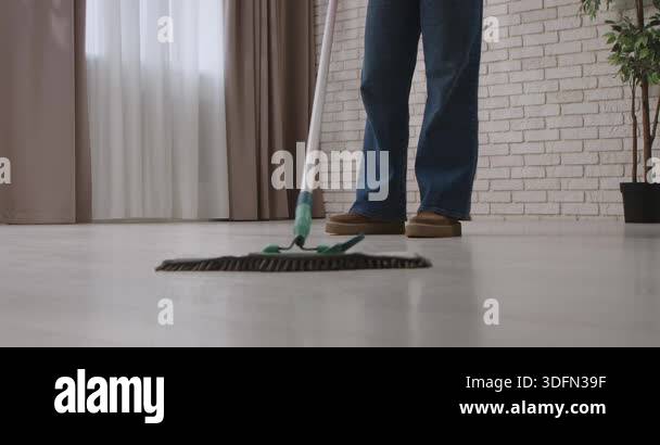 A person in blue jeans and slippers cleaning a bright room with a mop ...