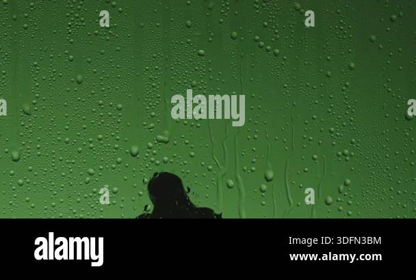 Silhouette of a finger drawing a heart on a foggy green glass surface ...