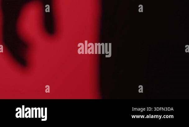 A dark shadow of a hand clenched into a fist against a red wall ...