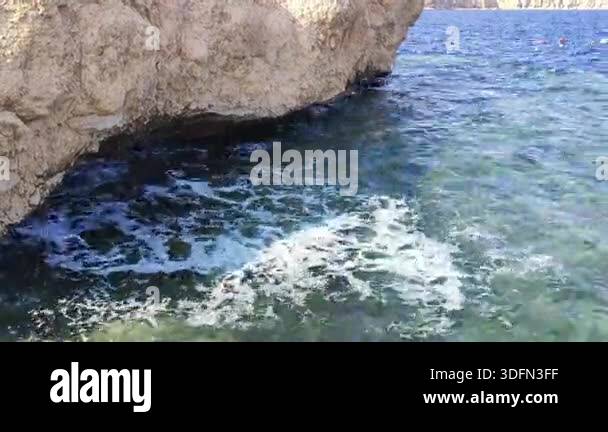 Ocean waves continuously crash against the rocky shore creating foam ...