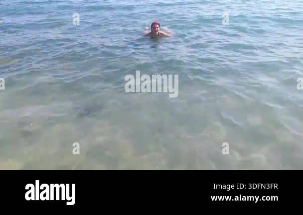 A woman swims energetically in clear water, creating splashes and ...
