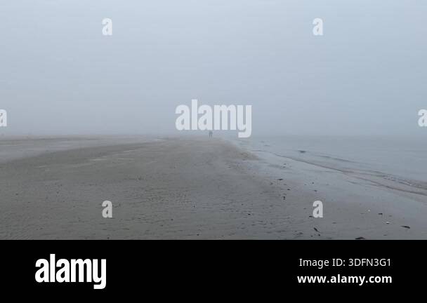A couple walking along the foggy, grey, empty beach on a cold winter ...