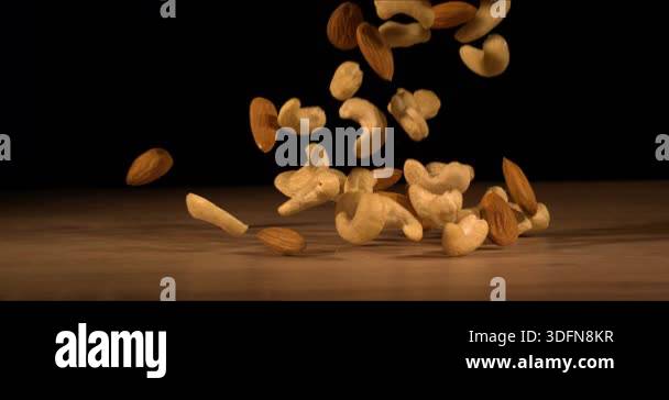 Super slow-motion of almonds and cashews fall on wooden table. Healthy ...