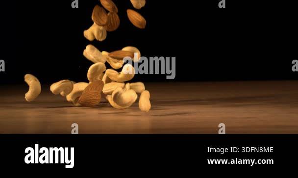 Super slow-motion of almonds and cashews fall on wooden table. Healthy ...