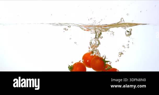 Slow-motion cherry tomatoes drop and splash into clear water ...
