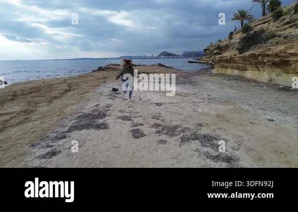 Aerial drone shot of a woman running along a rocky beach with her ...