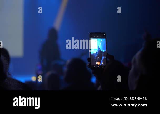 A hand holds a smartphone showing the stage and crowd while a musician ...