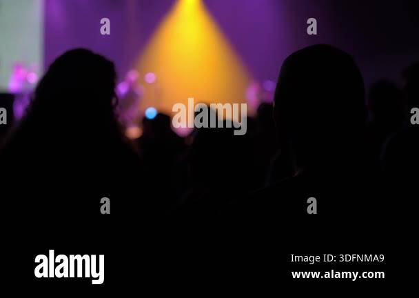 Dark silhouettes of concertgoers watch a performance with a bright ...