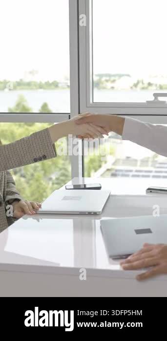 Man and woman shaking hands over a desk with laptops, sealing a deal in ...