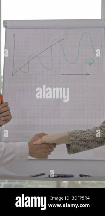 Man and woman shaking hands in agreement in front of a whiteboard with ...