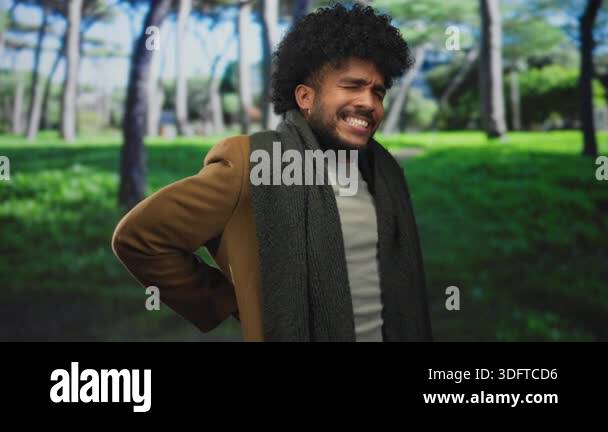 Man experiencing back pain in a green park outdoors, displaying ...