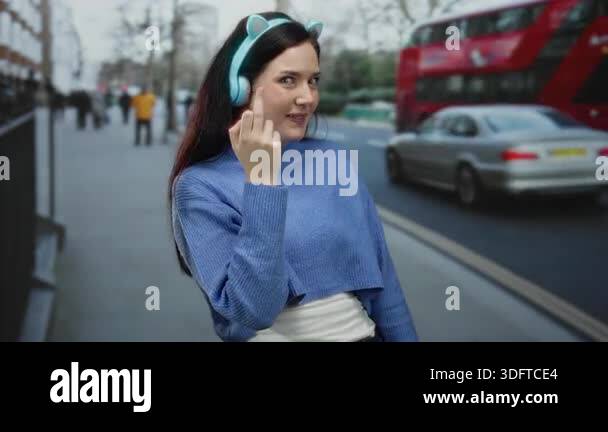 Woman showing middle finger with headphones while smiling on a city ...