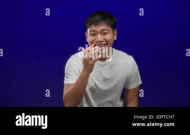 Young man covering face with hand while smiling against blue background ...