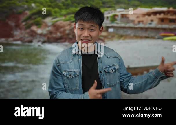 Young man in denim jacket standing by the seaside with vibrant green ...