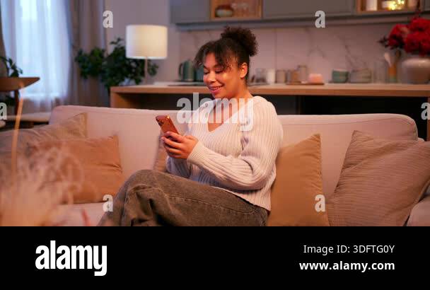 Smiling African American woman relaxing on the sofa while texting ...